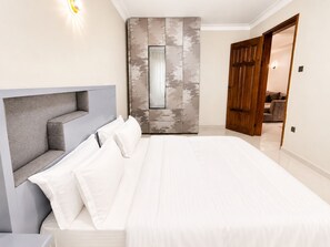 Quarto moderno com uma cama grande, um banco embutido, guarda-roupa e espelho.