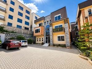 Um edifício residencial com vários andares, um pátio pavimentado, varandas e uma parede de pedra.