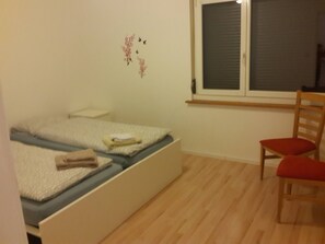 Quarto com cama, cadeira, janela e decoração na parede.