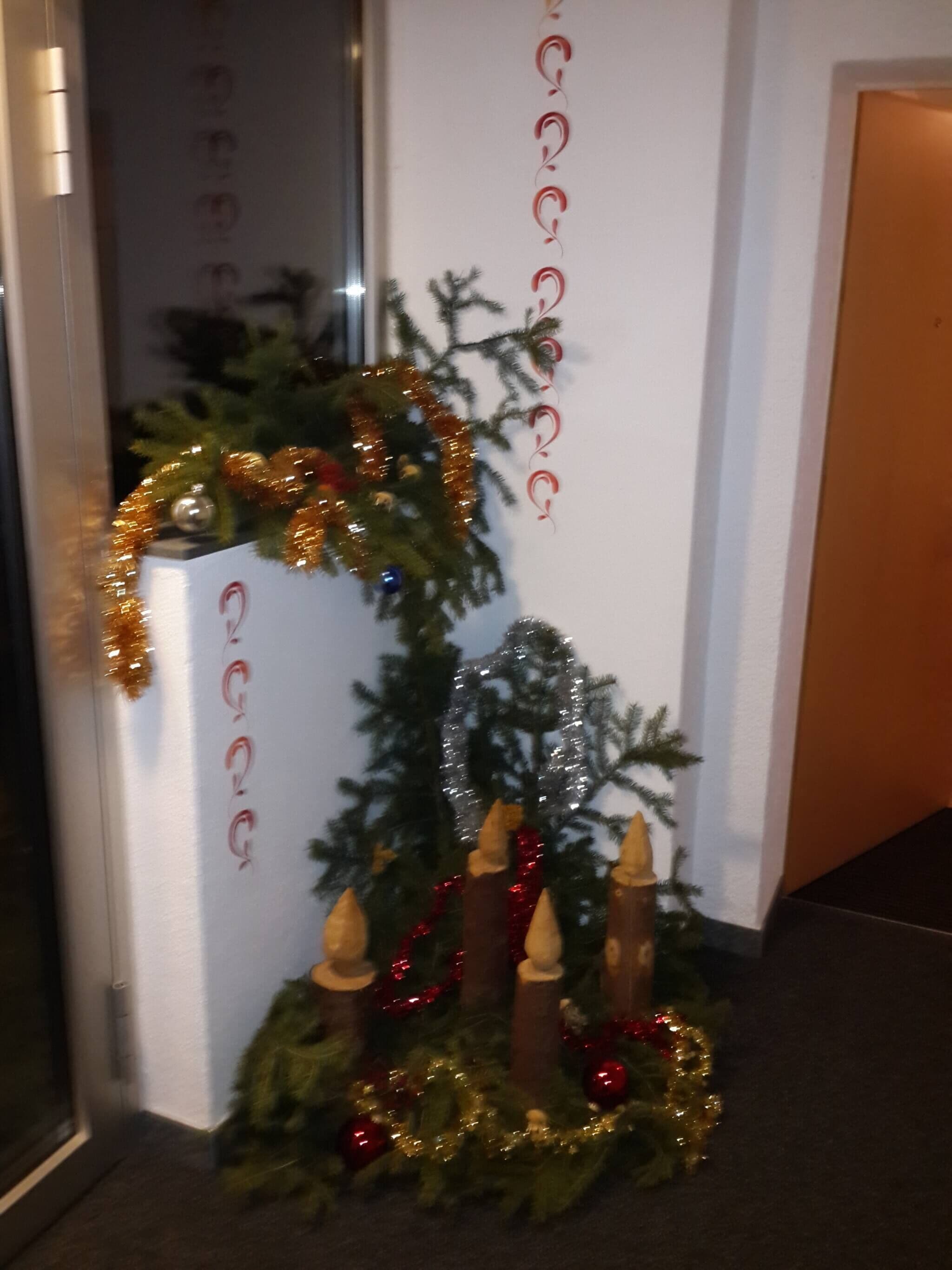 Uma árvore de Natal com enfeites e luzes, posicionada em frente a uma parede com decoração em letras decorativas.