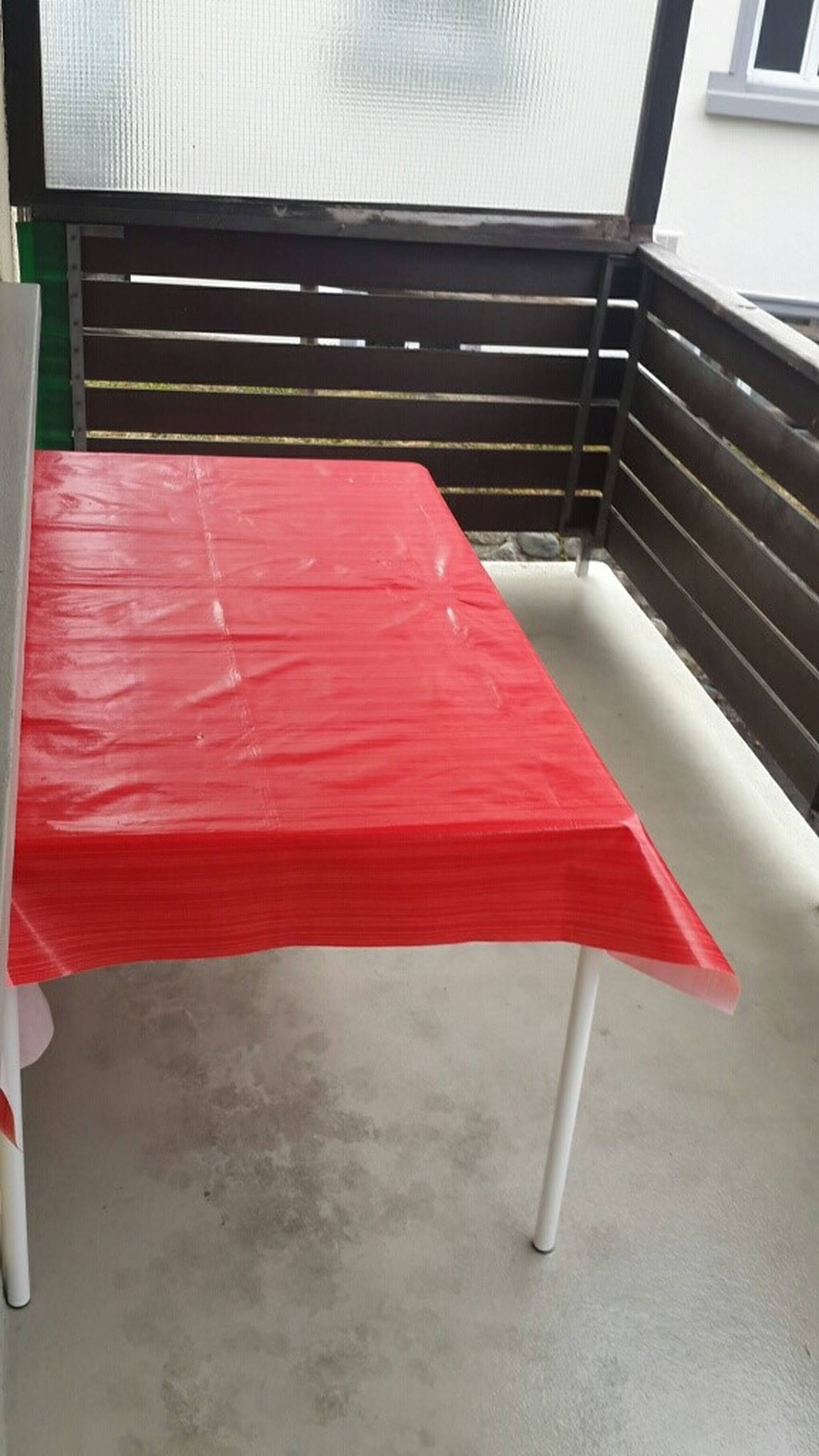 Uma mesa vermelha com pés brancos numa varanda.