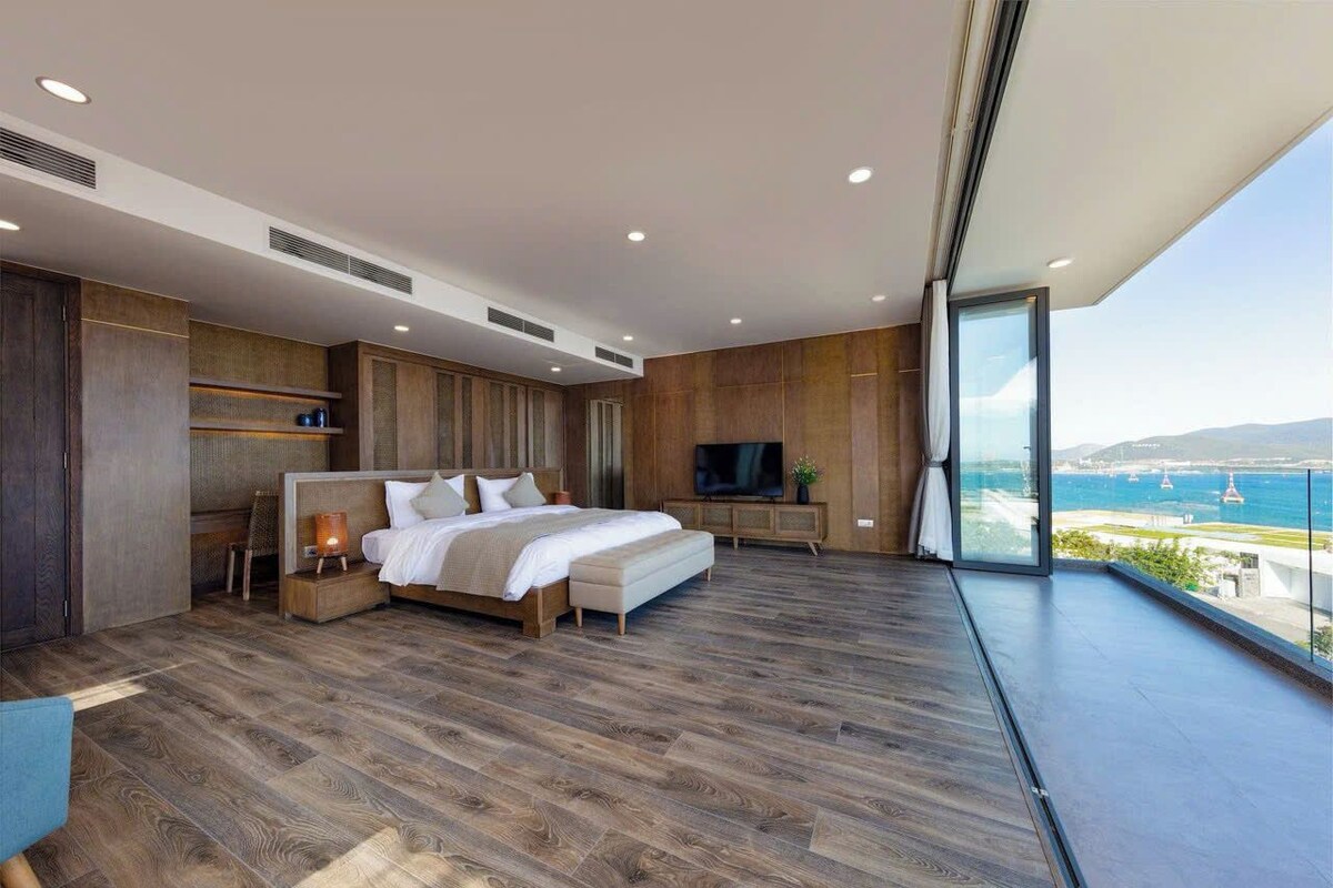 Quarto moderno com uma cama grande, televisão e vista para o mar.