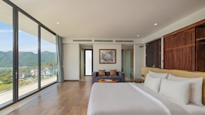 Quarto de hotel moderno com uma cama grande, área de estar com sofá e vista para as montanhas através de janelas do chão ao teto.