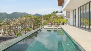 Uma piscina moderna com água cristalina, rodeada por vegetação exuberante e vista para montanhas ao longe.