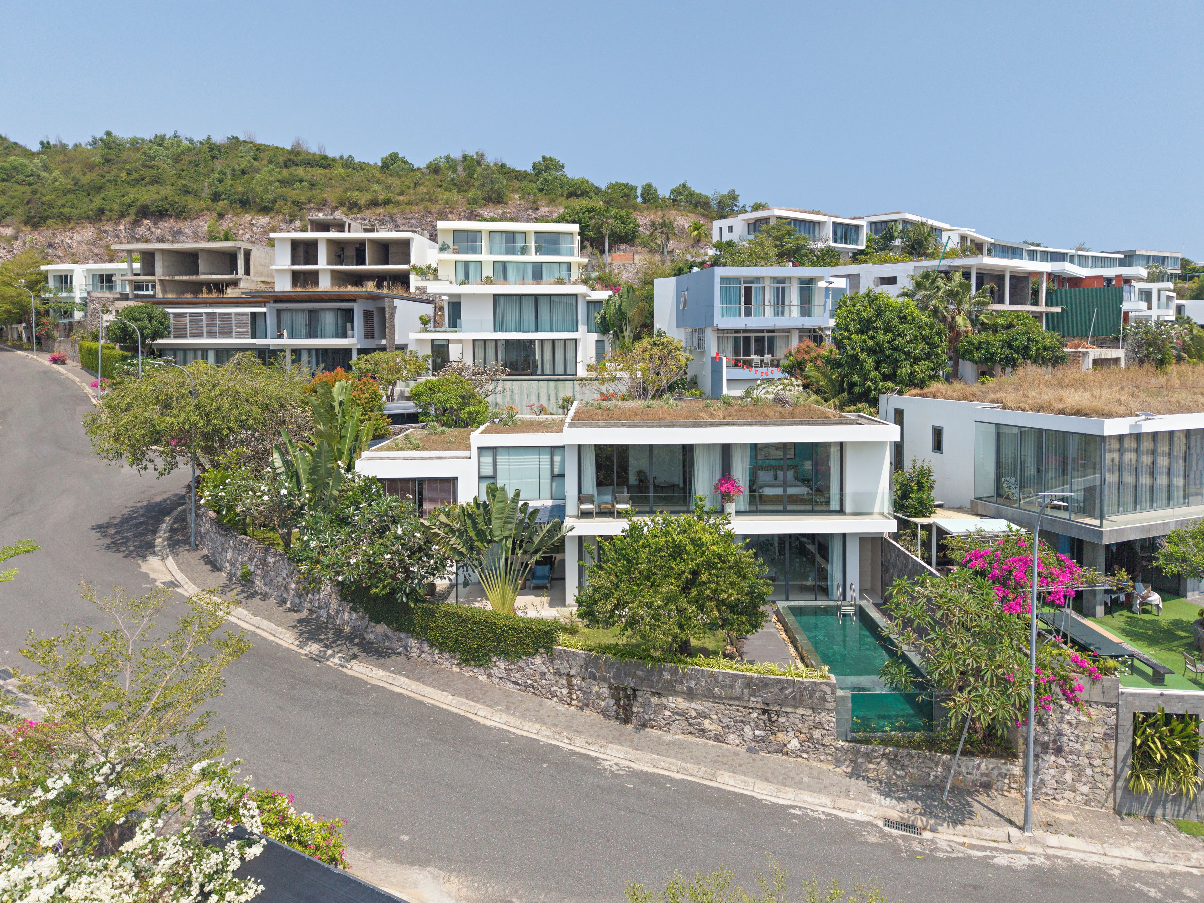 Zona residencial com casas modernas, janelas amplas e telhados planos, cercada por vegetação e céu limpo.
