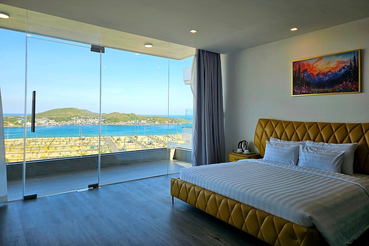 Quarto de hotel com uma cama grande, um quadro e vista para a praia e o mar.