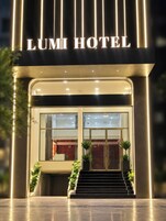 A entrada do HOTEL LUMI, com design moderno, apresenta uma fachada de vidro e uma escadaria que leva à entrada.