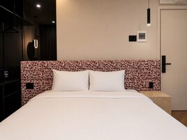 Quarto de hotel com cama, cabeceira com design estampado, porta e luminária fixa na parede.