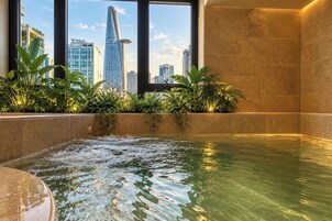 Uma banheira de hidromassagem com vista para a cidade, rodeada por plantas e uma parede revestida de azulejos.
