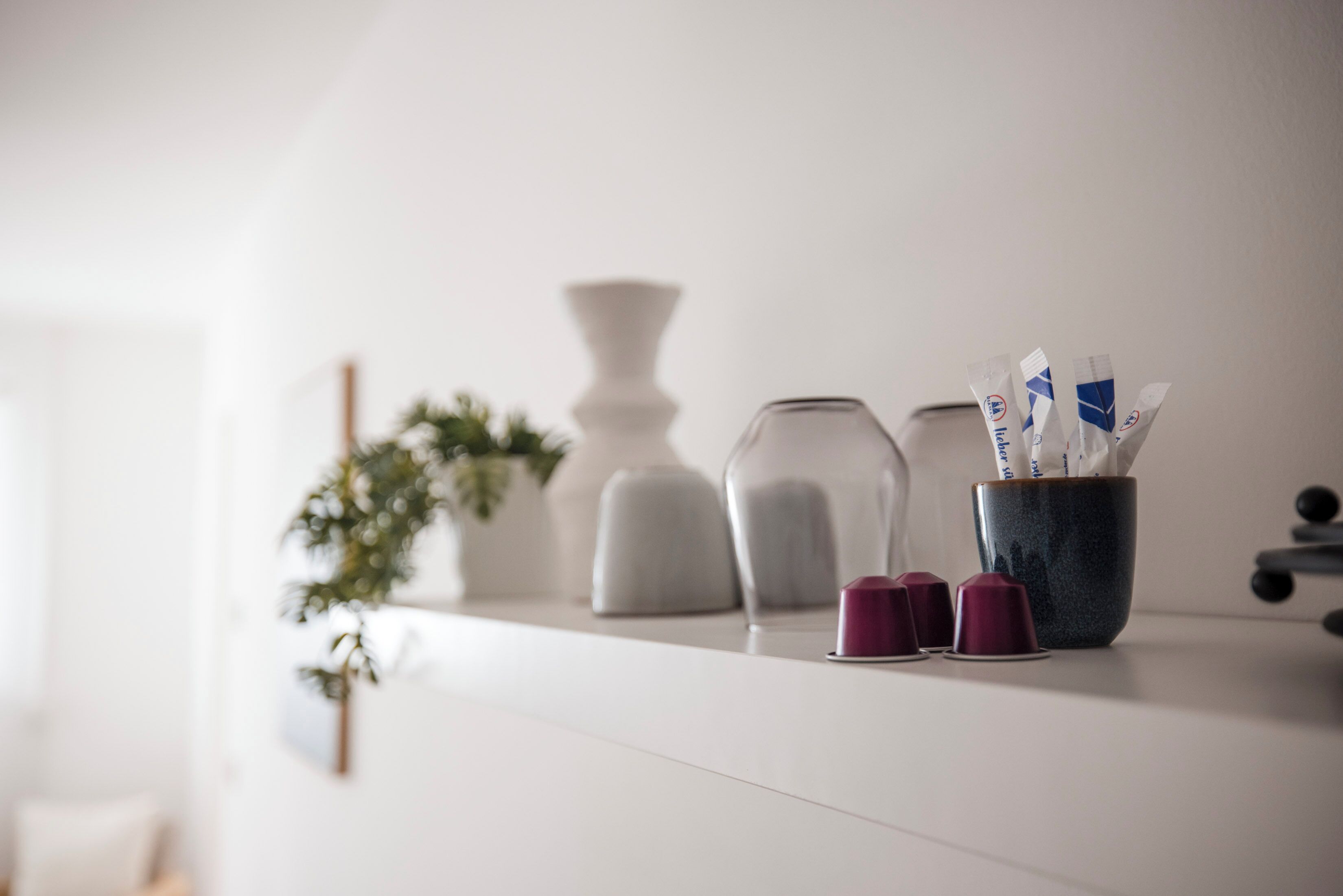 Uma prateleira branca com um vaso, um recipiente de vidro e uma caneca com lenços.