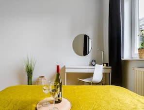 Quarto de hotel com cama, escrivaninha, cadeira, espelho, janela com cortinas e um vaso de planta.