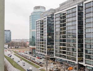 Um edifício de vários andares com fachada de vidro, estacionamento adjacente e uma rua com veículos.