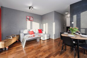 Uma sala de estar moderna com um sofá cinzento, uma mesa de centro e um espaço de jantar com mesa e cadeiras de madeira.