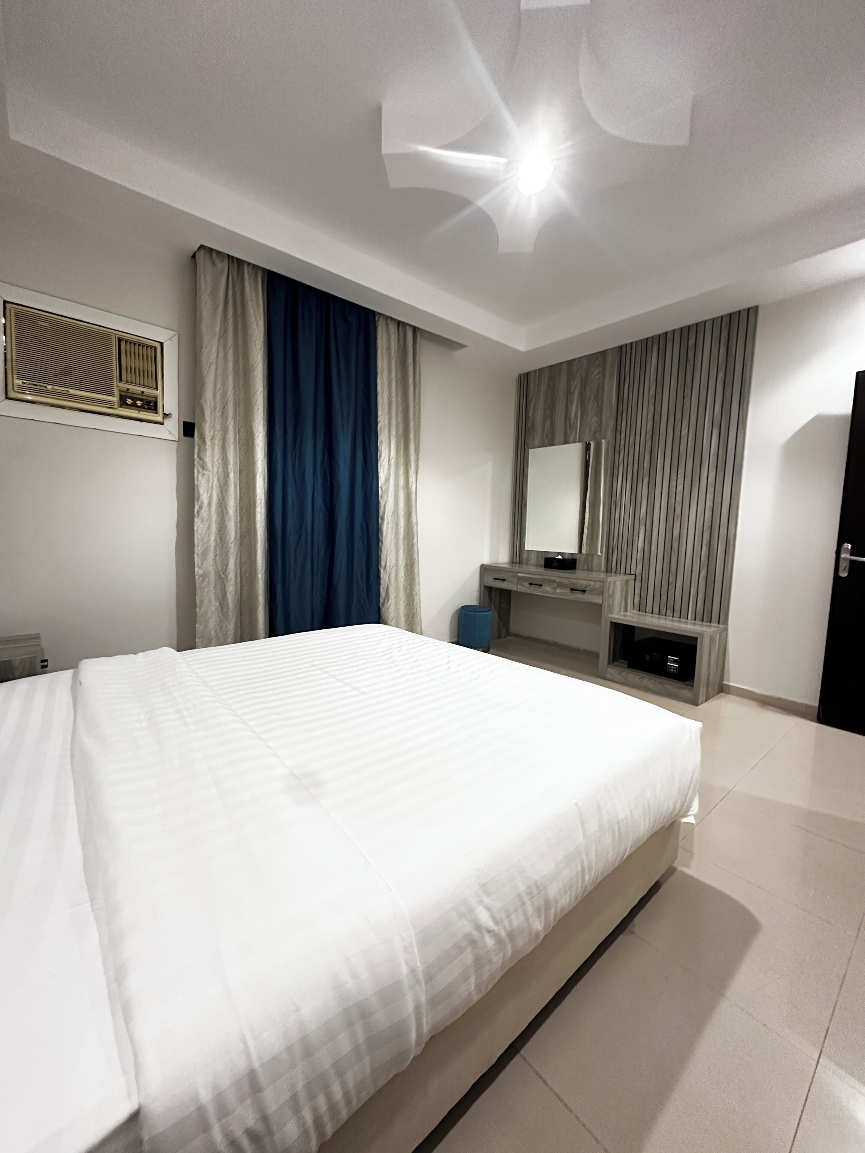 Quarto de hotel com uma cama grande, uma escrivaninha com cadeira, um espelho e um radiador.