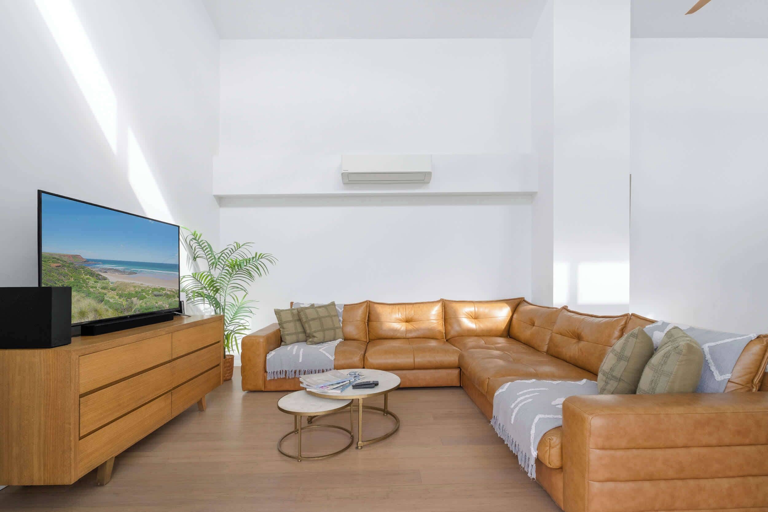 Uma sala de estar moderna com um sofá de couro, um móvel de TV em madeira e uma pequena mesa de centro redonda.