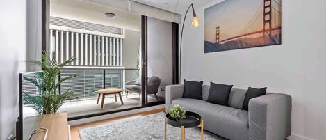 Uma sala de estar moderna com um sofá cinzento, uma mesa de centro, uma janela grande e um quadro de uma ponte.
