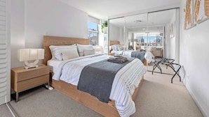 Quarto moderno com cama grande, mesas de cabeceira, espelho e vista para a cidade.