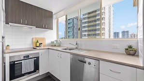 Uma cozinha moderna com armários brancos, lava-louças de aço inoxidável e uma janela com vista para a cidade.