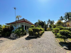 Uma casa com entrada por caminho de cascalho, cercada por jardins bem cuidados e palmeiras.