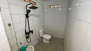 Uma casa de banho pequena com paredes revestidas a azulejos brancos, sanita, chuveiro com cabeça de duche manual e um balde verde.