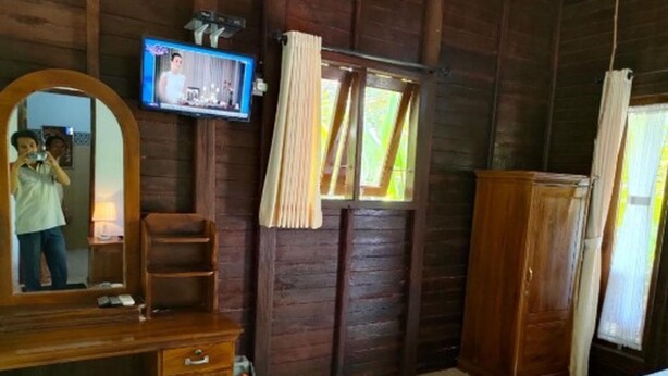 Um quarto de madeira com uma cama, cômoda, televisão fixada na parede e uma janela com cortinas.