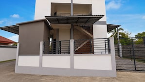 Edifício de vários andares com telhado plano, varanda no segundo andar e entrada com portão.