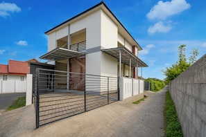 Uma casa moderna de dois andares com varanda coberta, entrada gradeada e acesso por alvenaria.