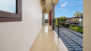Corredor limpo e moderno, com piso de azulejos brilhantes, guarda-corpo de metal à direita e vista desimpedida para o céu e vegetação lá fora.