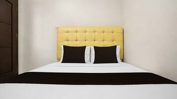 Uma cama de solteiro com cabeceira amarela estofada, roupa de cama branca e duas almofadas pretas.