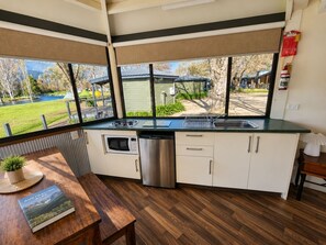 Cozinha compacta com vista para um parque, uma mesa de jantar com um livro e uma pequena planta em vaso.