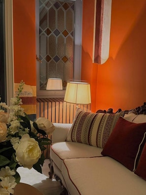 Quarto com sofá, luminária e janela com detalhe de vidro trabalhado.