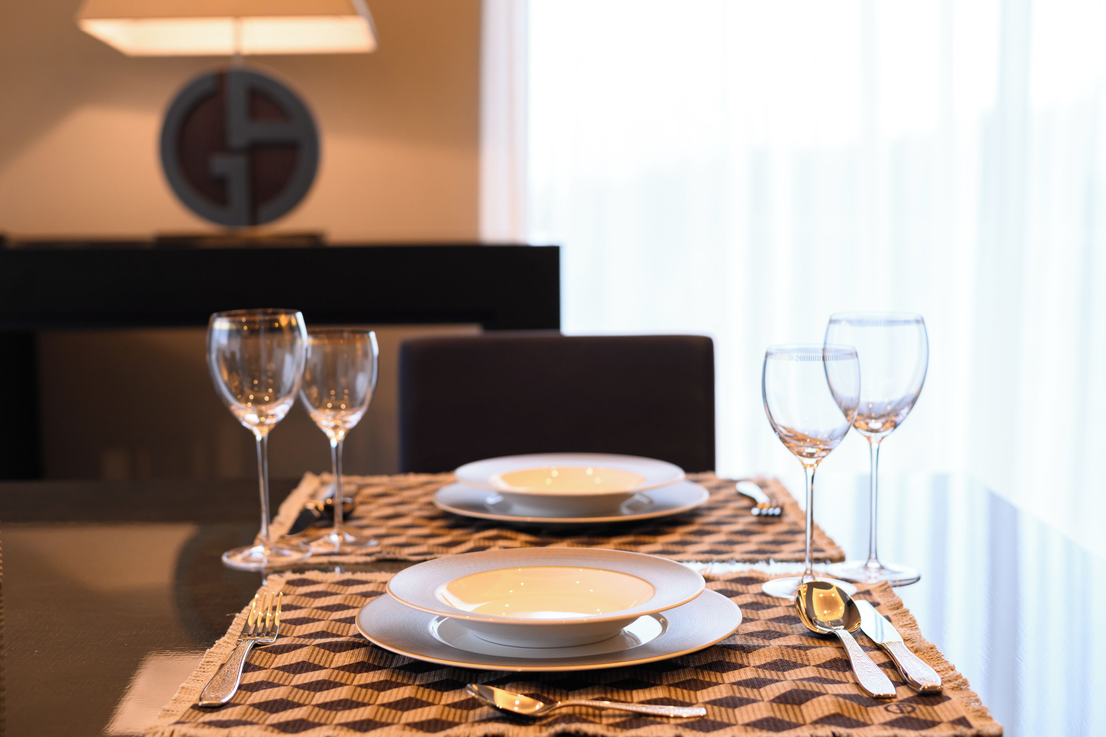 Uma mesa de jantar posta com pratos, copos, talheres e um jogo americano.