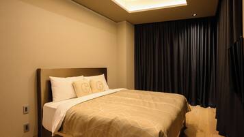 Quarto de hotel com uma cama, uma luminária no teto e uma cortina preta.