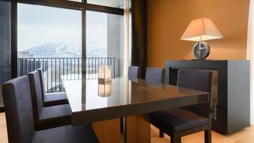 Uma sala de jantar moderna com uma mesa grande e cadeiras, lareira e vista para montanhas através de amplas janelas.