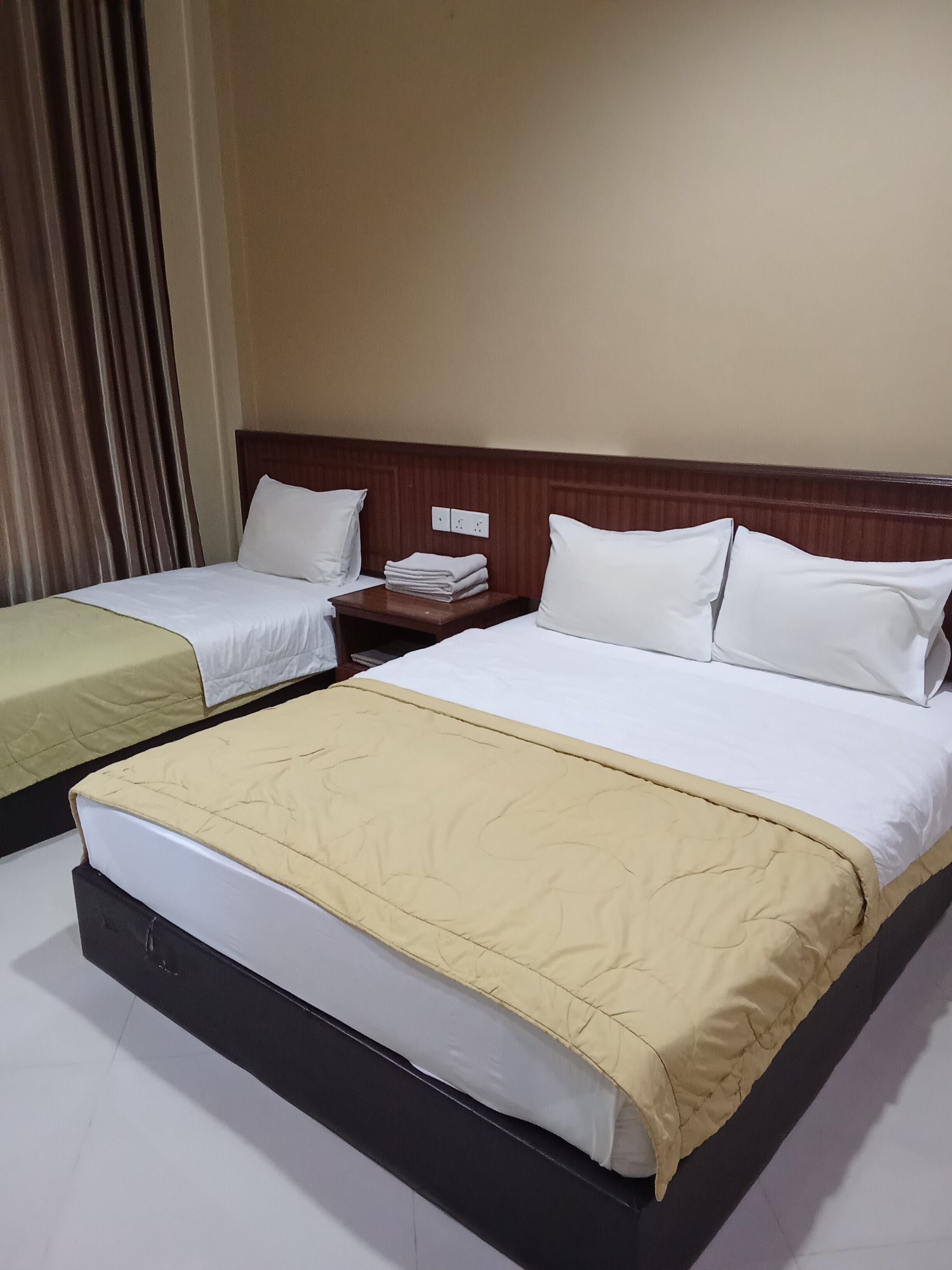 Quarto de hotel com duas camas, uma cabeceira de madeira e uma mesa de cabeceira com abajur.