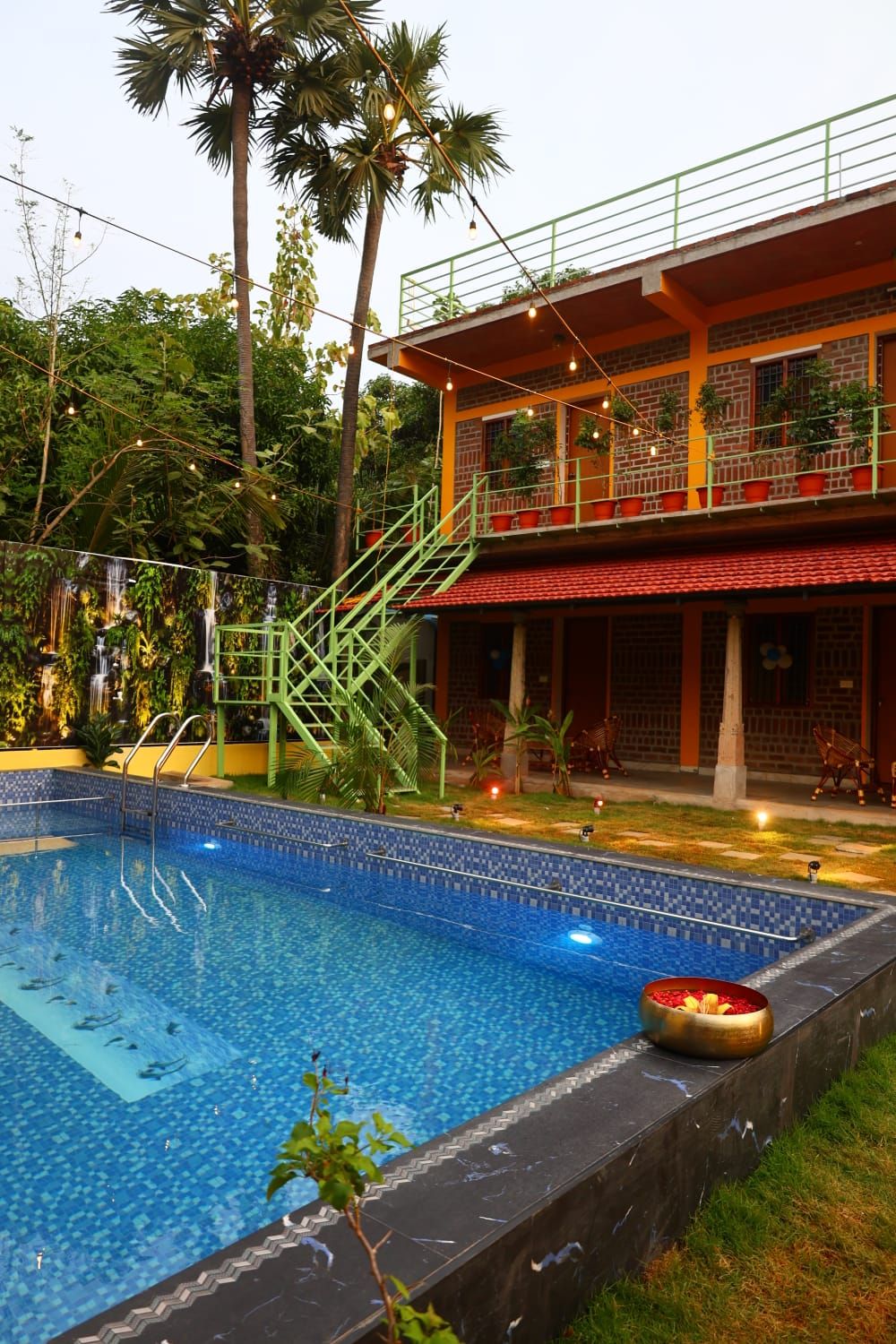 Piscina com borda azulejada, escadaria para uma varanda e um edifício com telhado vermelho e várias varandas.