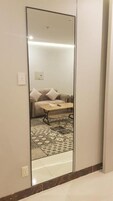 Quarto com um espelho grande refletindo um sofá, uma mesa pequena e um tapete estampado.