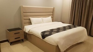 Uma cama com cabeceira, uma mesa de cabeceira com gavetas e um cobreleiro estampado sobre a cama.