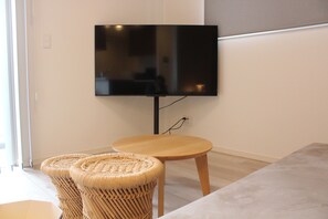 Uma sala de estar moderna com uma televisão de tela plana na parede, uma mesa de madeira redonda e duas cadeiras de vime trançado.