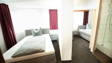 Quarto de hotel com cama, sofá, mesa de cabeceira e chuveiro.