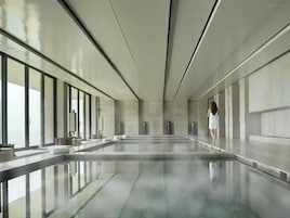 Uma piscina interior ampla com paredes de vidro transparente, design moderno e uma pessoa passando.