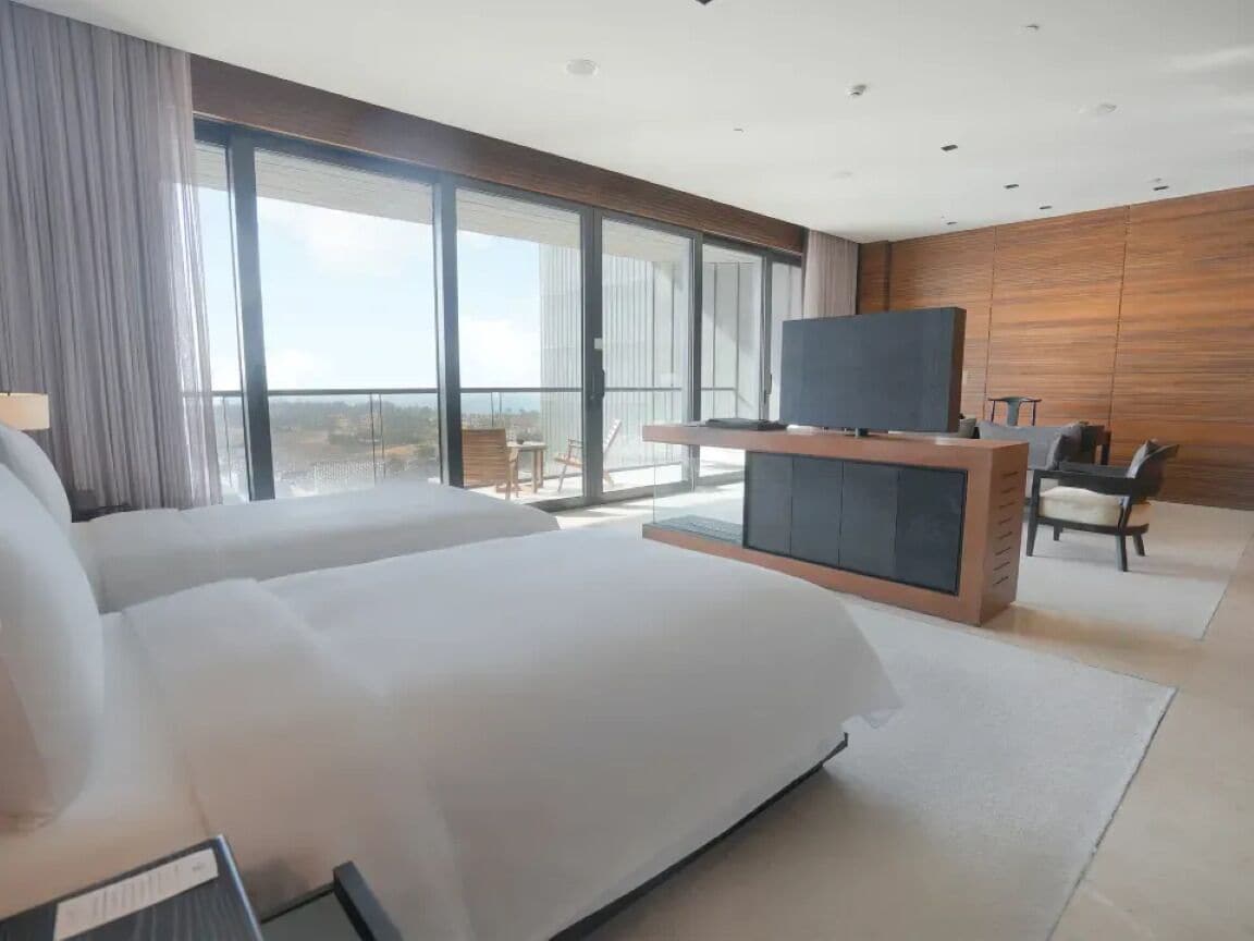 Quarto de hotel moderno com uma cama grande, uma TV de tela plana em um suporte de madeira e uma varanda com vista.