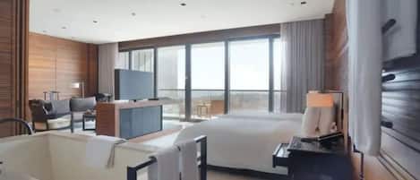 Quarto de hotel com uma cama grande, área de estar com escrivaninha e cadeira, banheira e televisão.