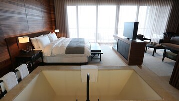 Quarto de hotel com uma cama grande, uma escrivaninha, uma televisão, um sofá e uma banheira.