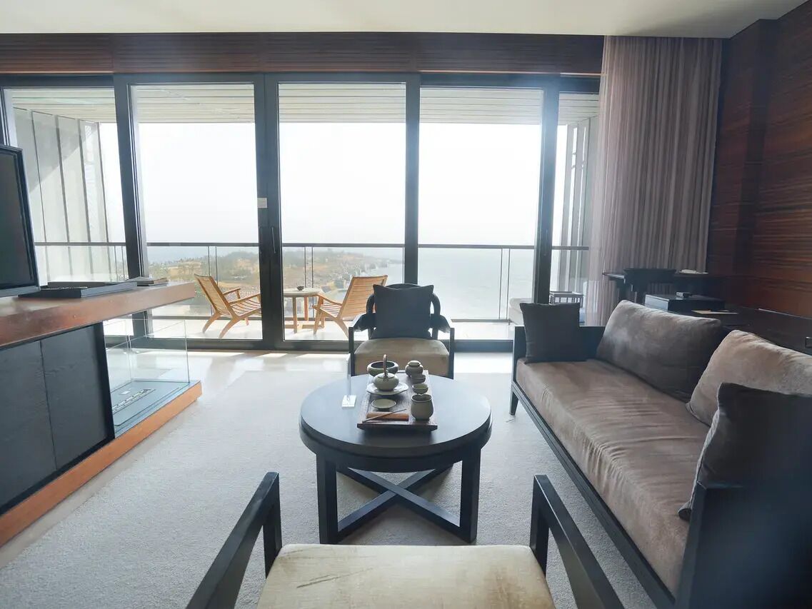 Uma sala de estar moderna com sofá, mesa de centro e cadeiras, televisão e varanda com vista.