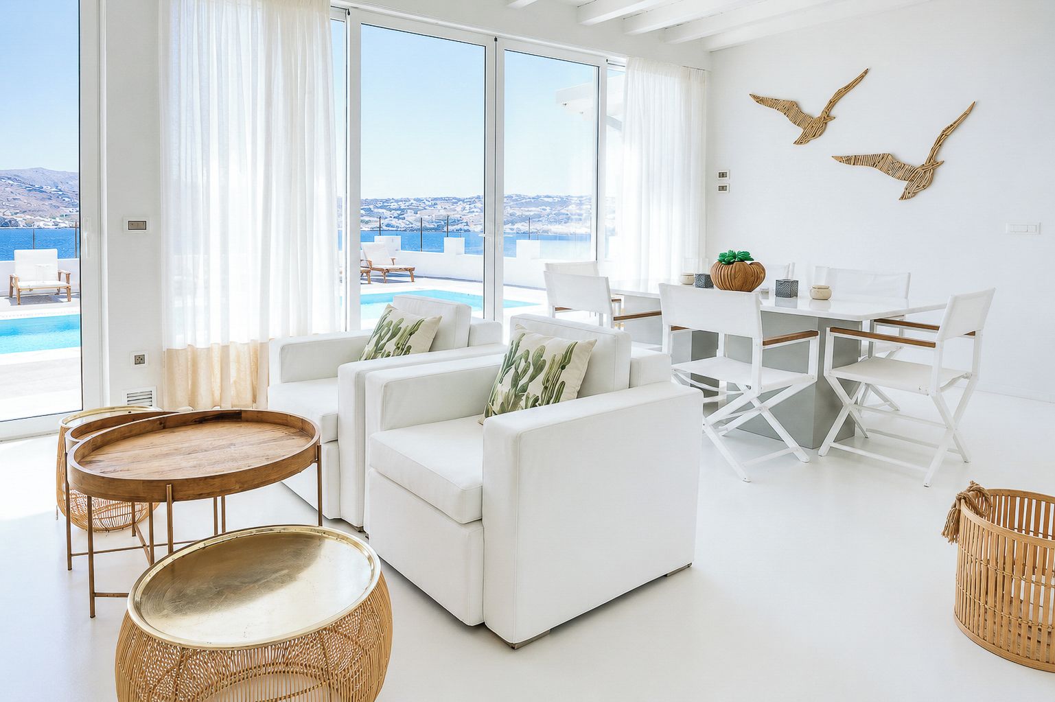 Sala moderna vista para o mar, mobiliário branco e área de jantar.
