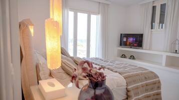 Quarto de hotel com uma cama, televisão, um vaso com flores e uma janela com cortinas.