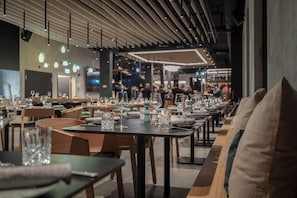 Interior de restaurante com várias mesas, cadeiras e luminárias pendentes.