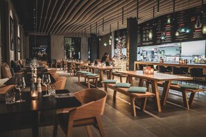 Um restaurante com mesas e cadeiras de madeira, um espaço de bar e um quadro de cardápio.