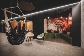 Um interior moderno com uma cadeira de rede, um sofá verde e um mural na parede.